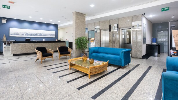 Um lobby moderno com balcão de recepção, área de estar e uma grande pintura da paisagem urbana na parede.