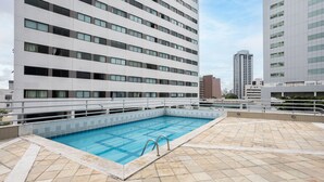 Uma piscina no terraço com um deck ladrilhado, rodeada por edifícios altos.