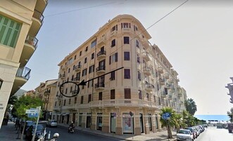 Um edifício com várias andares e varandas, com uma rua na frente e carros estacionados.