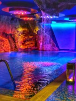 Piscina com cascata iluminada por luzes coloridas.