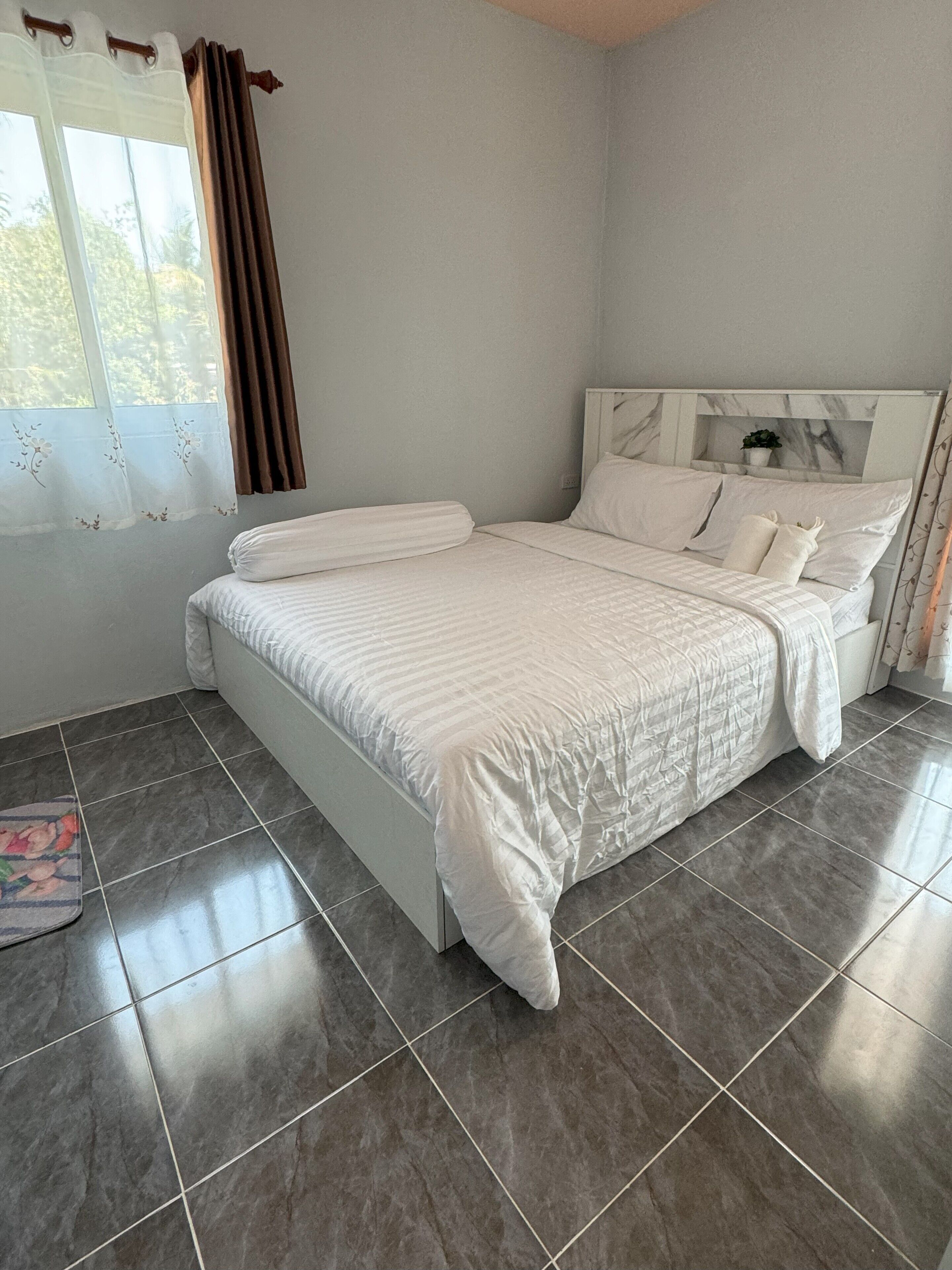Uma cama bem arrumada com roupa de cama branca, uma cabeceira de mármore e uma janela com cortinas.