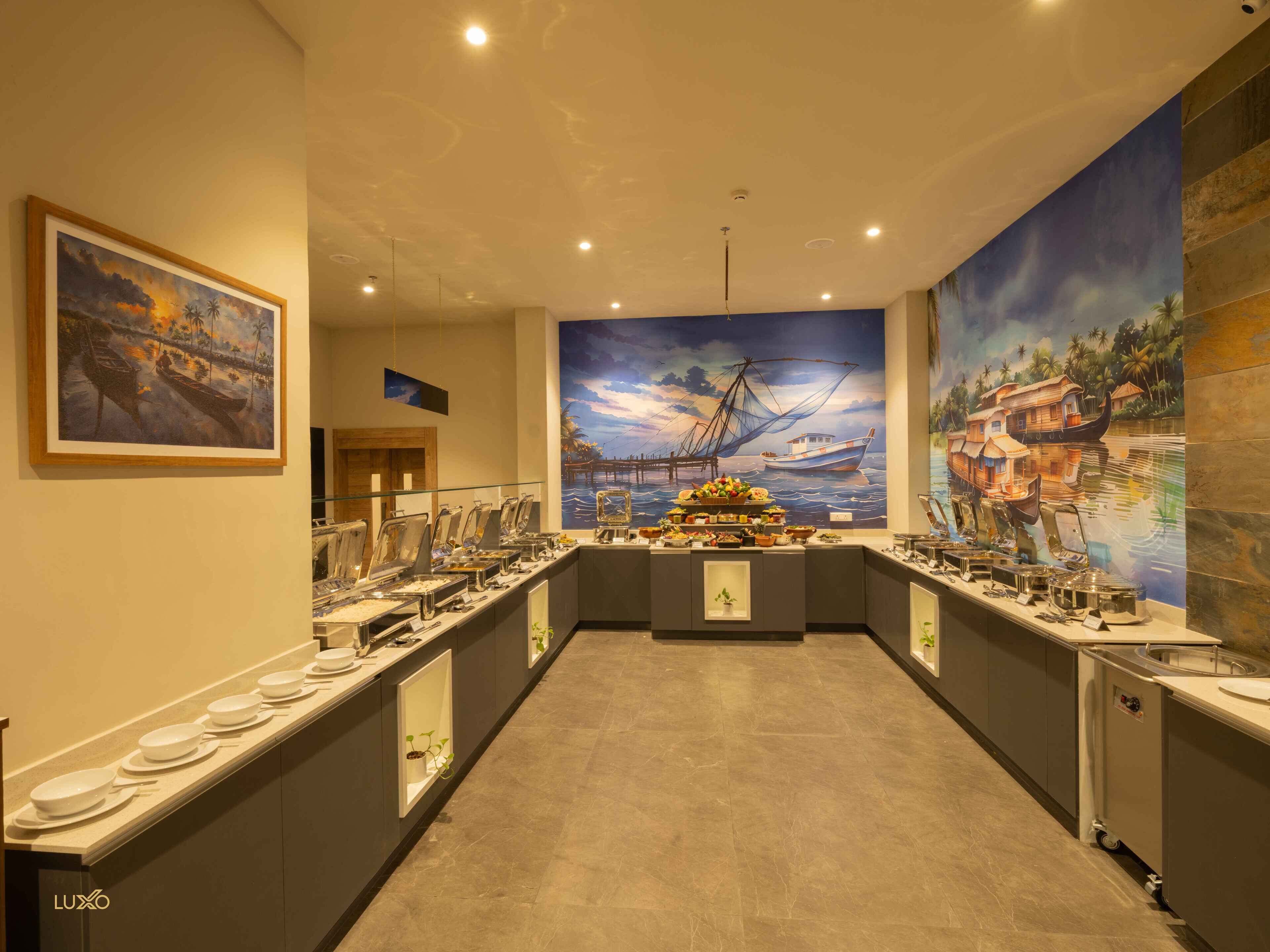 Uma área de buffet com um balcão extenso, diversas estações de serviço e um mural retratando uma cena tropical com barcos e casas.