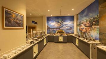Uma área de buffet com um balcão extenso, diversas estações de serviço e um mural retratando uma cena tropical com barcos e casas.