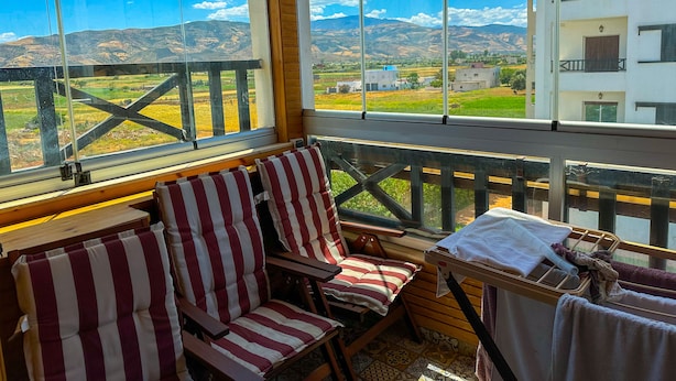 Quarto com grandes janelas que oferecem vista para montanhas e campos, móveis de madeira e uma mesa com um varal.