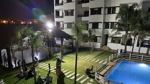 Um pátio com piscina, palmeiras e área de estar coberta.