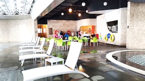 Um espaço interior moderno com poltronas brancas e mesas verdes, uma área de estar central com um banco curvo, e um chão estampado.