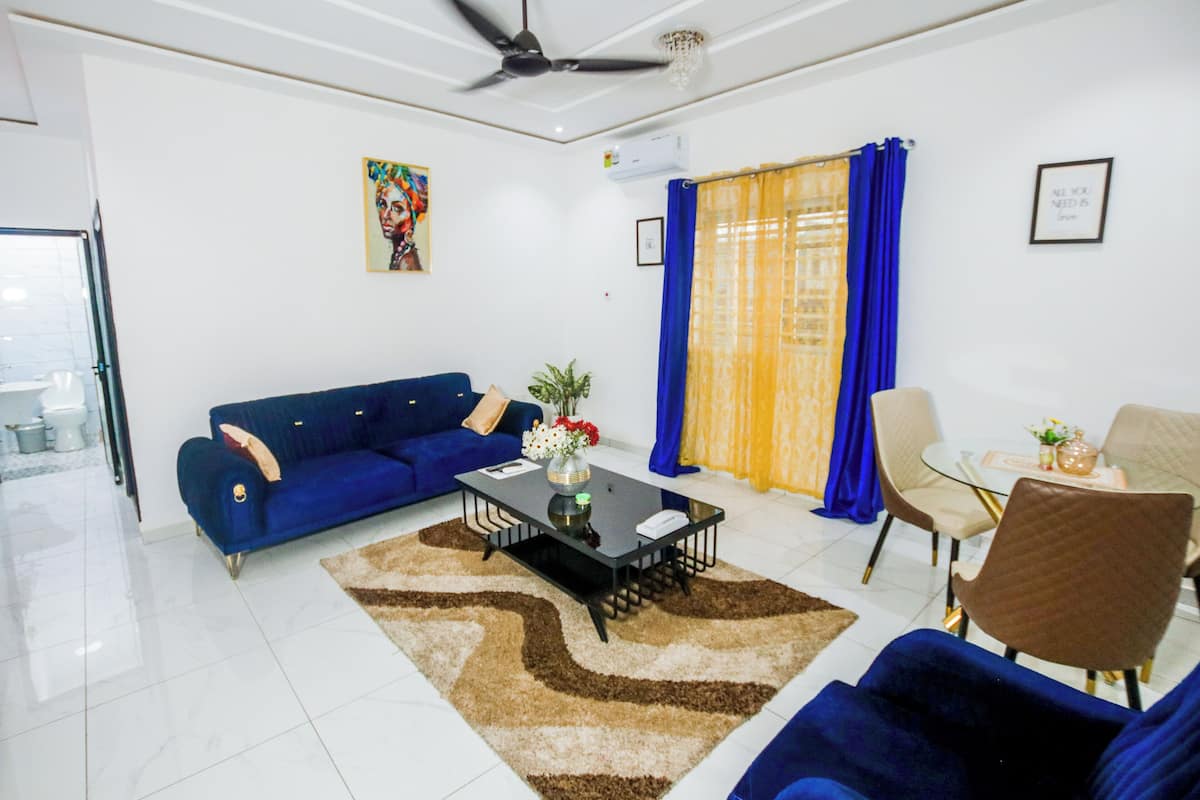 Uma sala de estar moderna com um sofá azul, uma mesa de centro e um espaço de jantar com uma mesa de vidro e cadeiras.