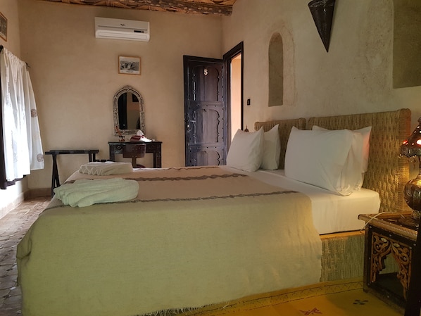 Quarto com cama, cabeceira de madeira, mesa de cabeceira, espelho e porta.