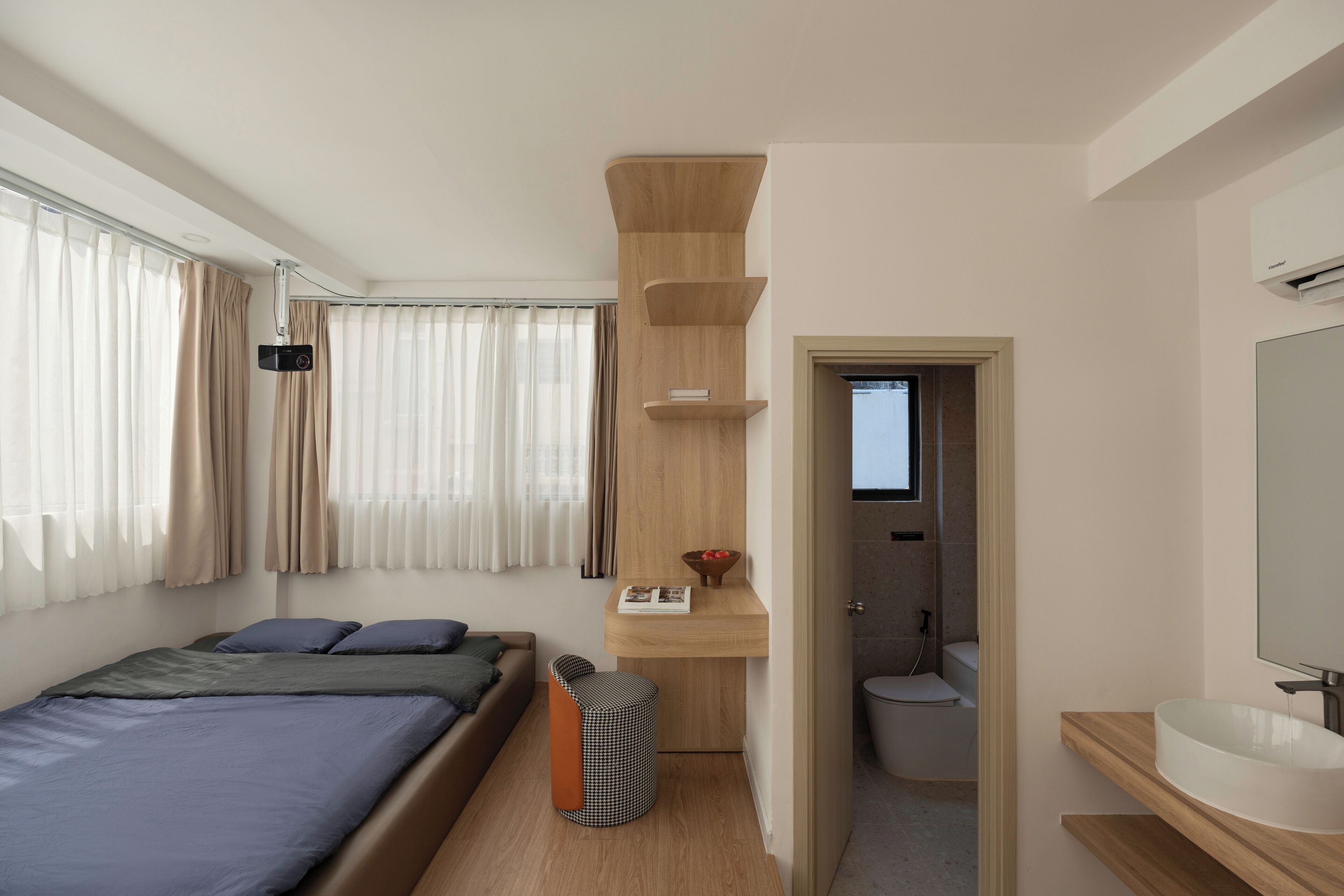 Quarto de hotel moderno com uma cama, mesa de cabeceira e um banheiro visível por uma porta aberta.