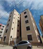 Um edifício residencial de vários andares com fachada bege, várias janelas e uma cerca de metal em primeiro plano.