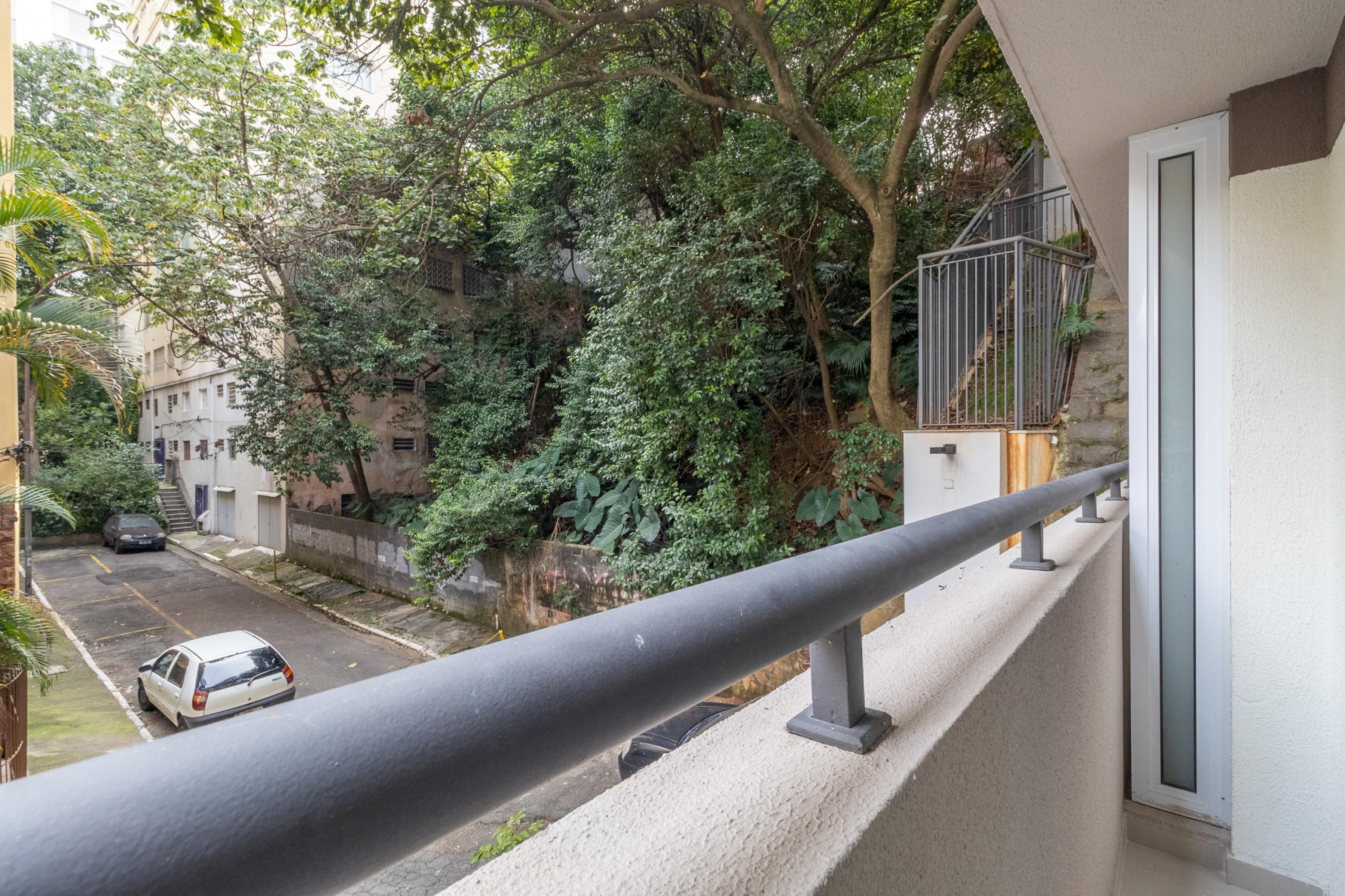 Varanda com grade de metal, vista para uma rua com carros estacionados e árvores.