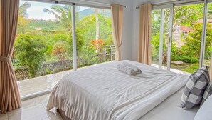 Quarto com cama grande, cortinas e vista para o verde lá fora.