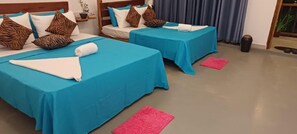 Duas camas de solteiro com colchas azuis, almofadas brancas e cabeceira de madeira.
