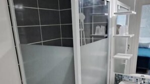 Uma casa de banho com sanita, chuveiro em cabine de vidro e lavatório.