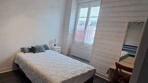 Quarto com cama, mesa de cabeceira, cadeira e janela.