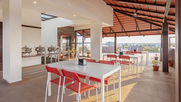 Uma área de refeições ao ar livre ampla, com cadeiras vermelhas e brancas, uma mesa branca e um sistema de buffet.