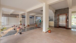 Um hall amplo com piso em azulejos, várias plantas em vasos, uma escada e um elevador moderno.