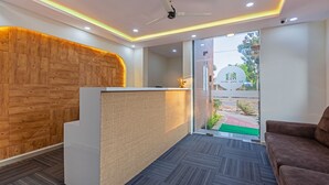 Uma área de recepção com parede de madeira, balcão de atendimento, sofá e porta de vidro que dá para o exterior.