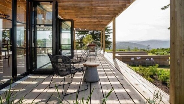 Um deck de madeira ao ar livre com assentos e uma porta de vidro que dá para um interior moderno.