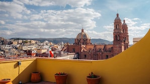 Terraço no telhado com vasos de terracota e vista para um edifício histórico com cúpulas e um campanário.