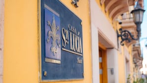 Uma placa para 'Casa St Lucia' em um edifício amarelo, com um ornamento de metal decorativo acima.