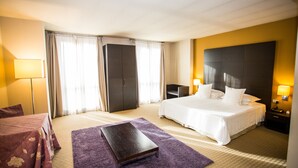 Quarto de hotel com cama, escrivaninha, cadeira, mesa de cabeceira, abajur e guarda-roupa.
