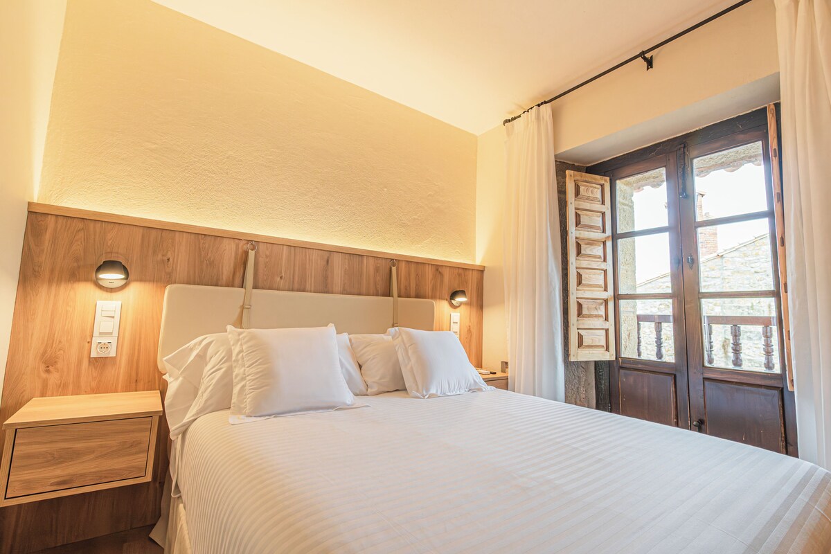 Uma cama bem arrumada com lençóis brancos, uma cabeceira de madeira e duas luminárias laterais.