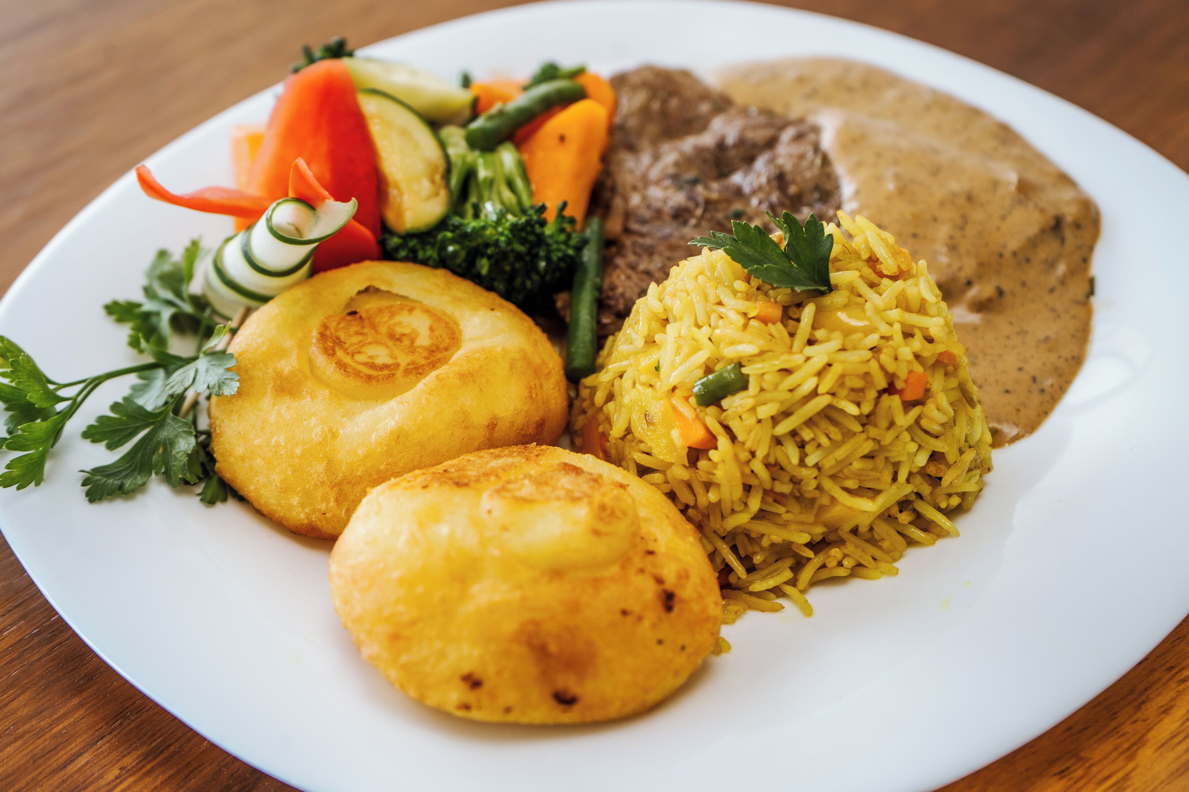 Prato de comida com arroz, carne, legumes e pães.