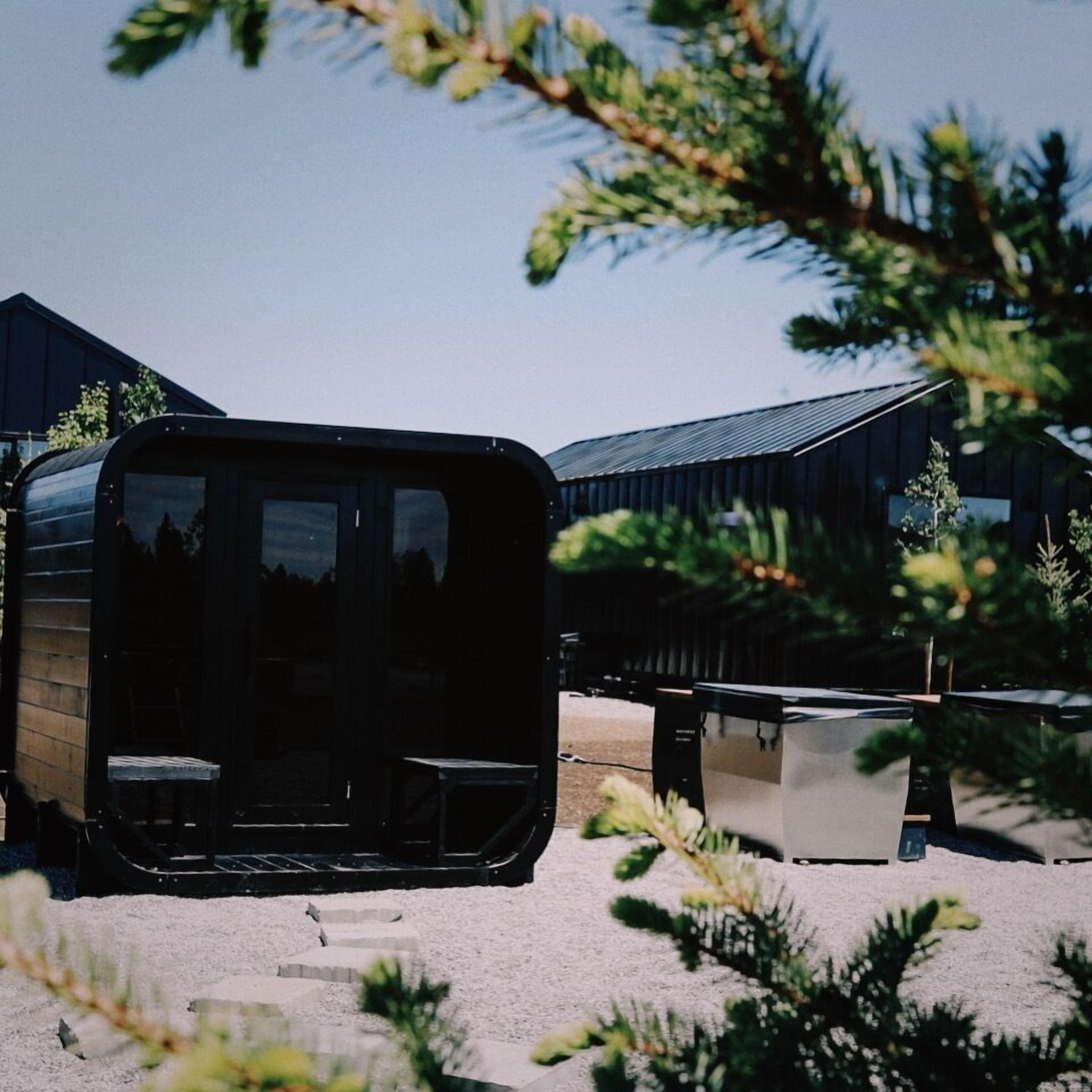 Um edifício moderno com design minimalista, apresentando uma grande estrutura preta com janelas e um prédio menor adjacente com telhado inclinado.