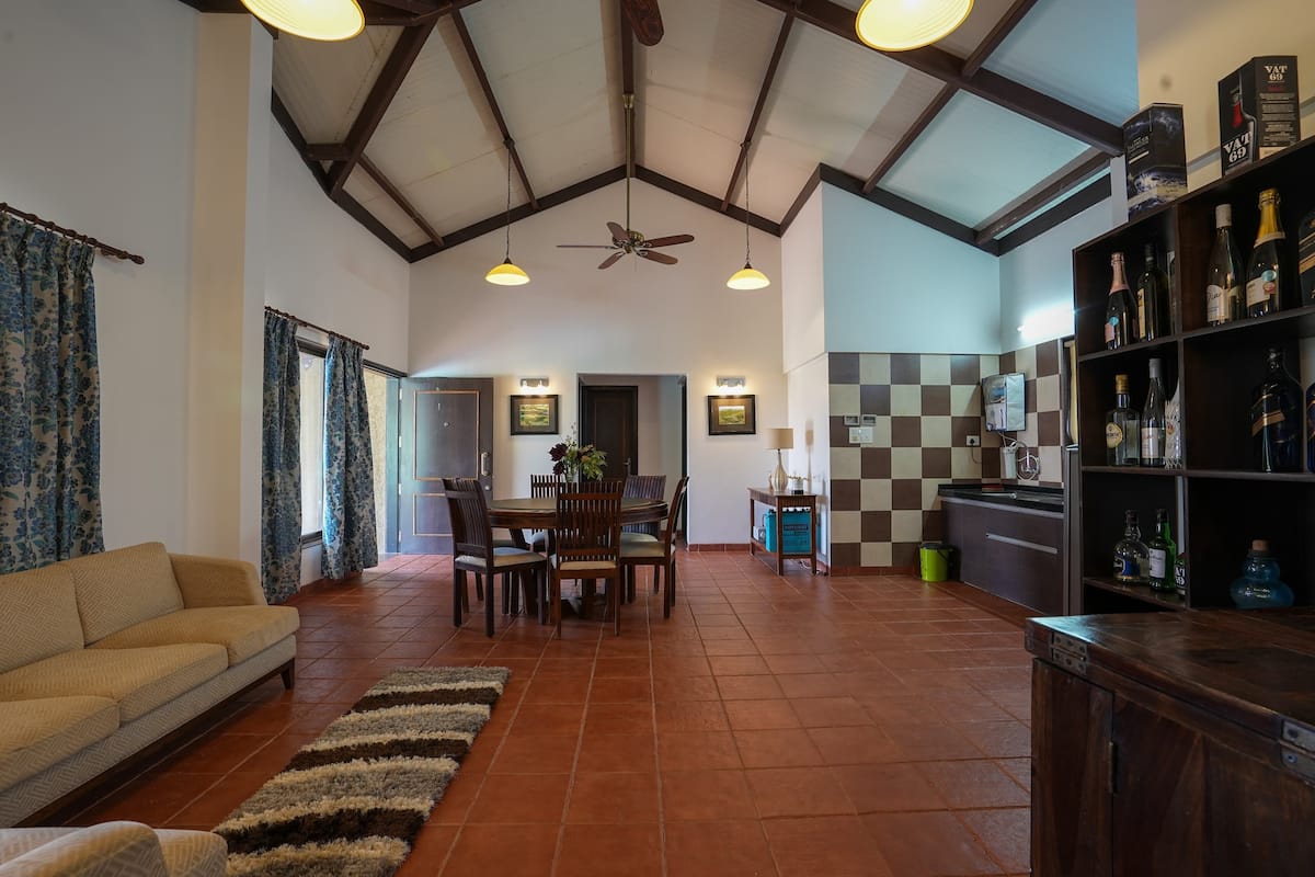 Uma sala de estar espaçosa com teto alto, área de jantar e cozinha com detalhes xadrez no revestimento.