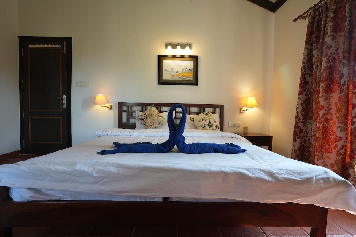 Uma cama bem arrumada com uma escultura de toalha, duas luminárias na parede, um quadro emoldurado e uma porta.