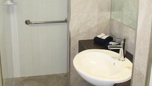 Casa de banho com cabine de chuveiro em vidro, lavatório branco, porta-toalhas e espelho.