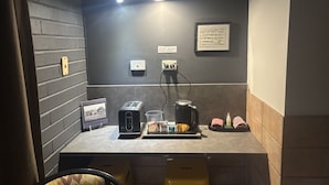Uma pequena cozinha compacta com torradeira, chaleira e um quadro na parede.