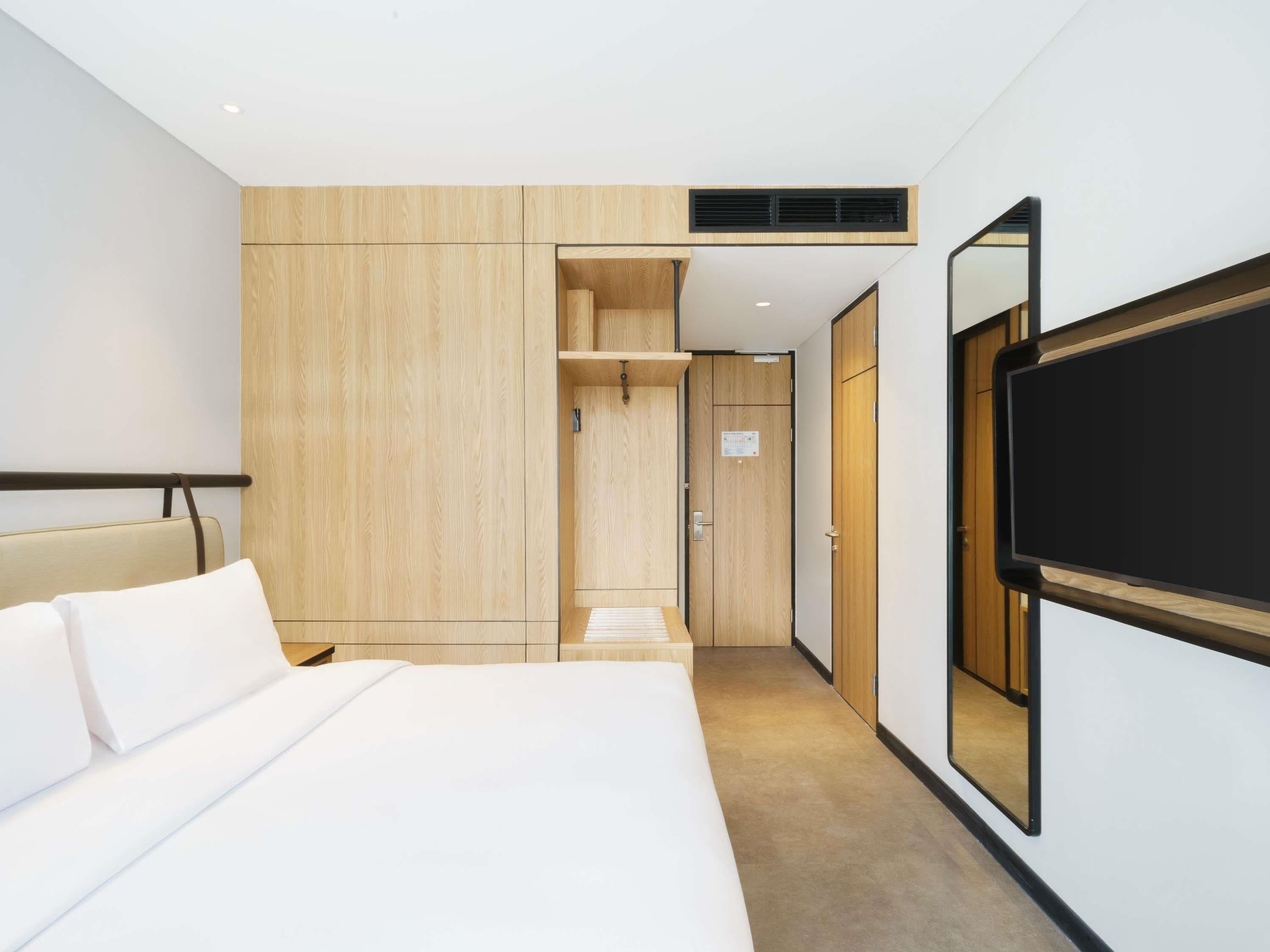 Quarto de hotel moderno com uma cama grande, guarda-roupa de madeira, televisão e espelho.