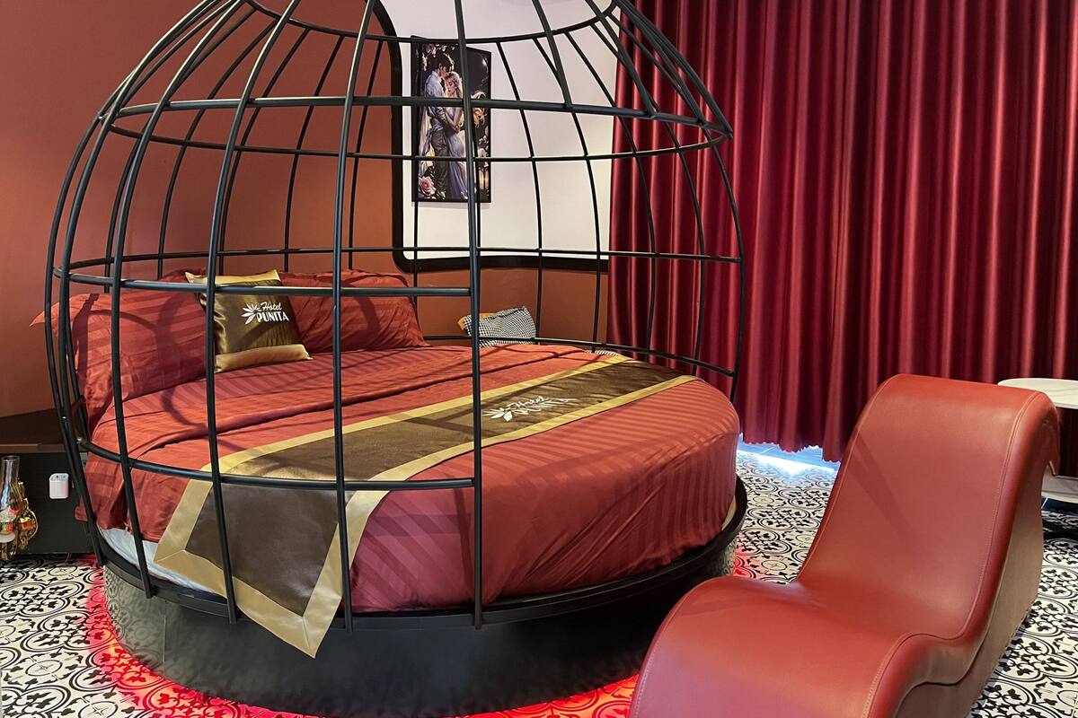 Uma cama redonda com estrutura de metal, roupa de cama vermelha e um travesseiro com logotipo.