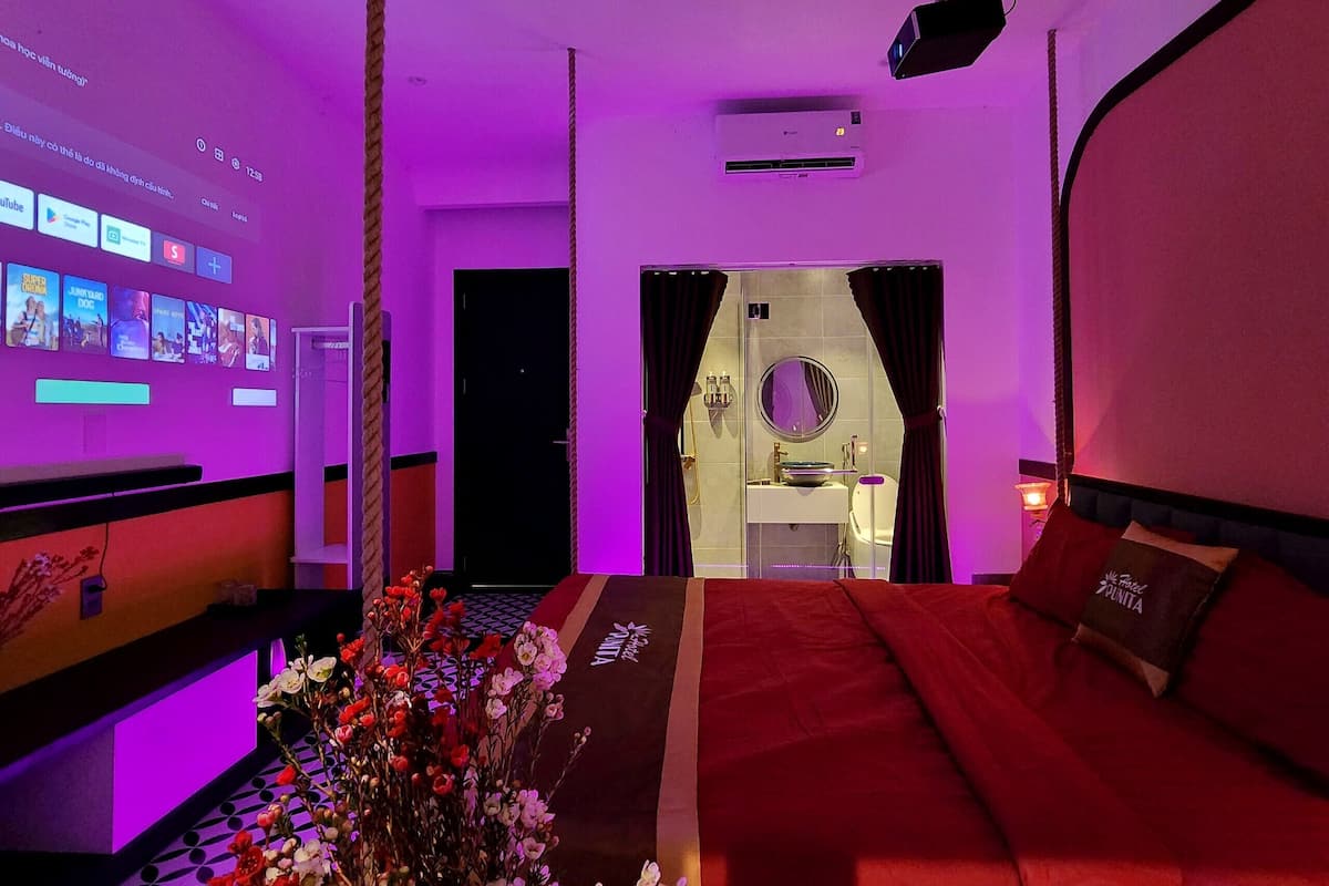 Quarto de hotel com cama, escrivaninha e televisão exibindo um menu de serviço de quarto.