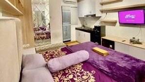 Quarto moderno com cama, televisão e cozinha compacta.