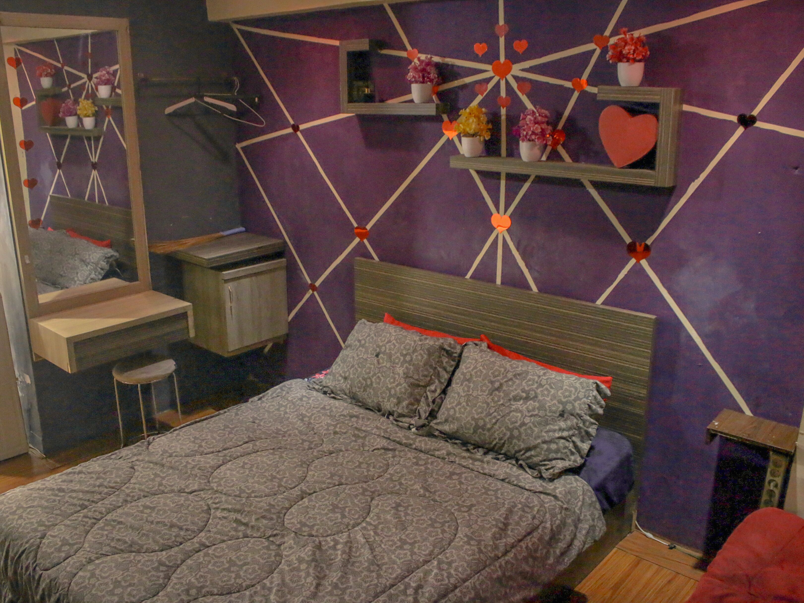 Quarto com cama, cômoda, penteadeira e parede com padrão geométrico e decoração de corações.
