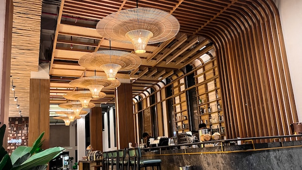 Uma área de bar moderna com vigas de madeira no teto, luminárias de vime pendentes e bancada de mármore.