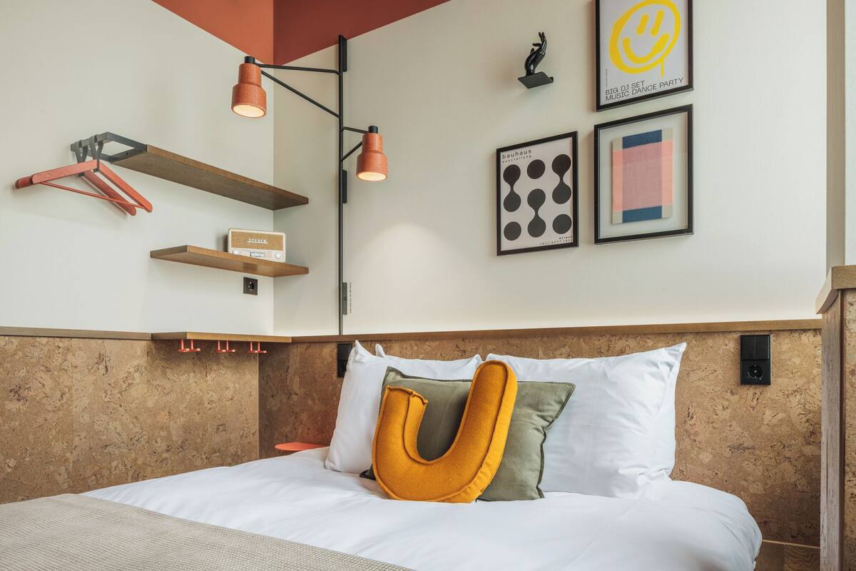 Quarto de hotel moderno com cama, travesseiro em U grande, rádio e obra de arte na parede.