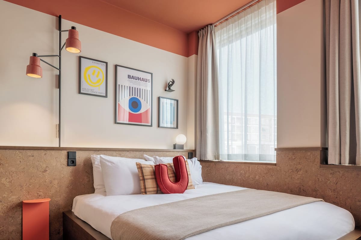 Quarto de hotel com cama, mesa de cabeceira, luminária fixada na parede e obras de arte emolduradas.