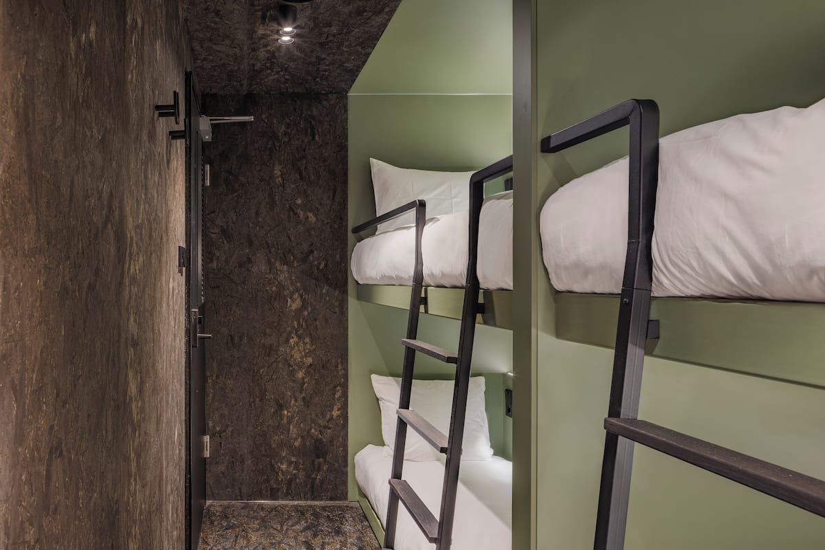 Uma cama beliche com roupa de cama branca e uma escada, uma porta de madeira e uma parede com textura.