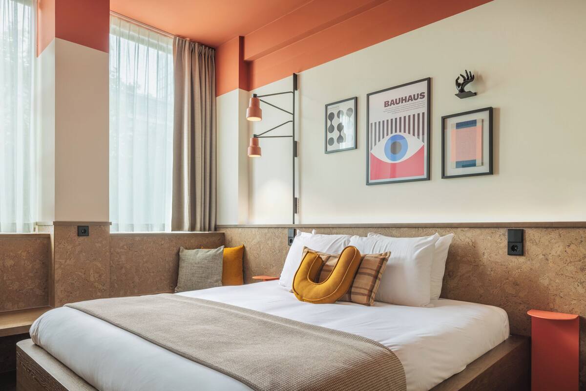 Quarto de hotel com uma cama grande, janela com cortinas e obras de arte na parede.
