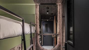 Um corredor estreito com beliches em uma parede e uma porta no final.