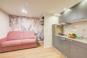 Cozinha moderna com armários cinza, um sofá rosa e papel de parede floral.