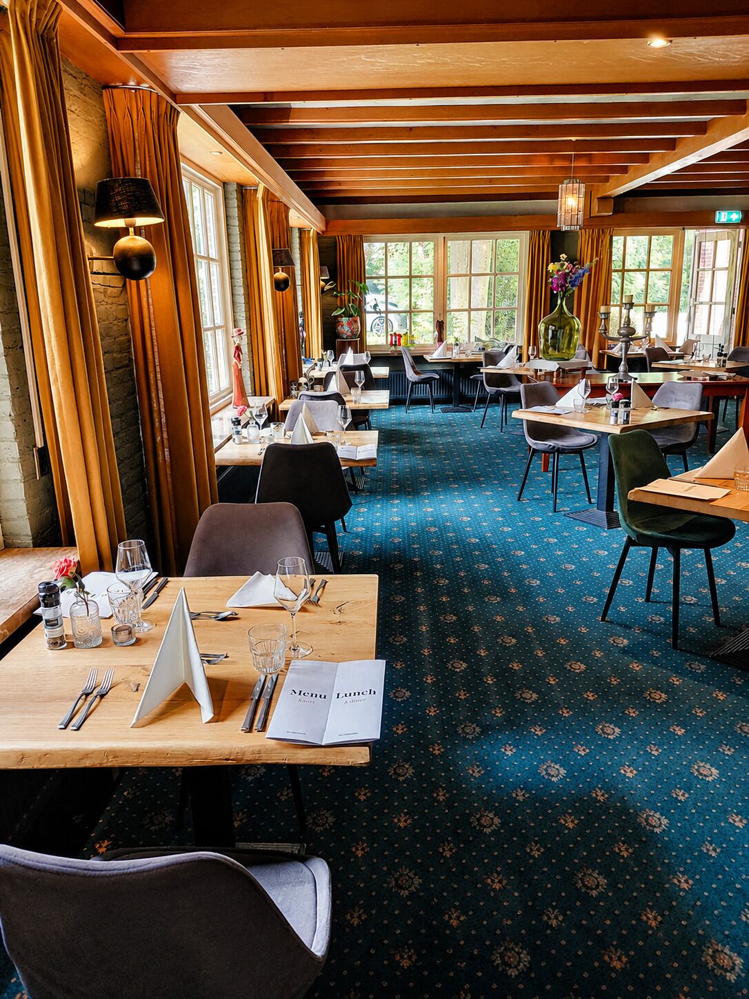 Restaurante com várias mesas, cadeiras e um tapete azul estampado.