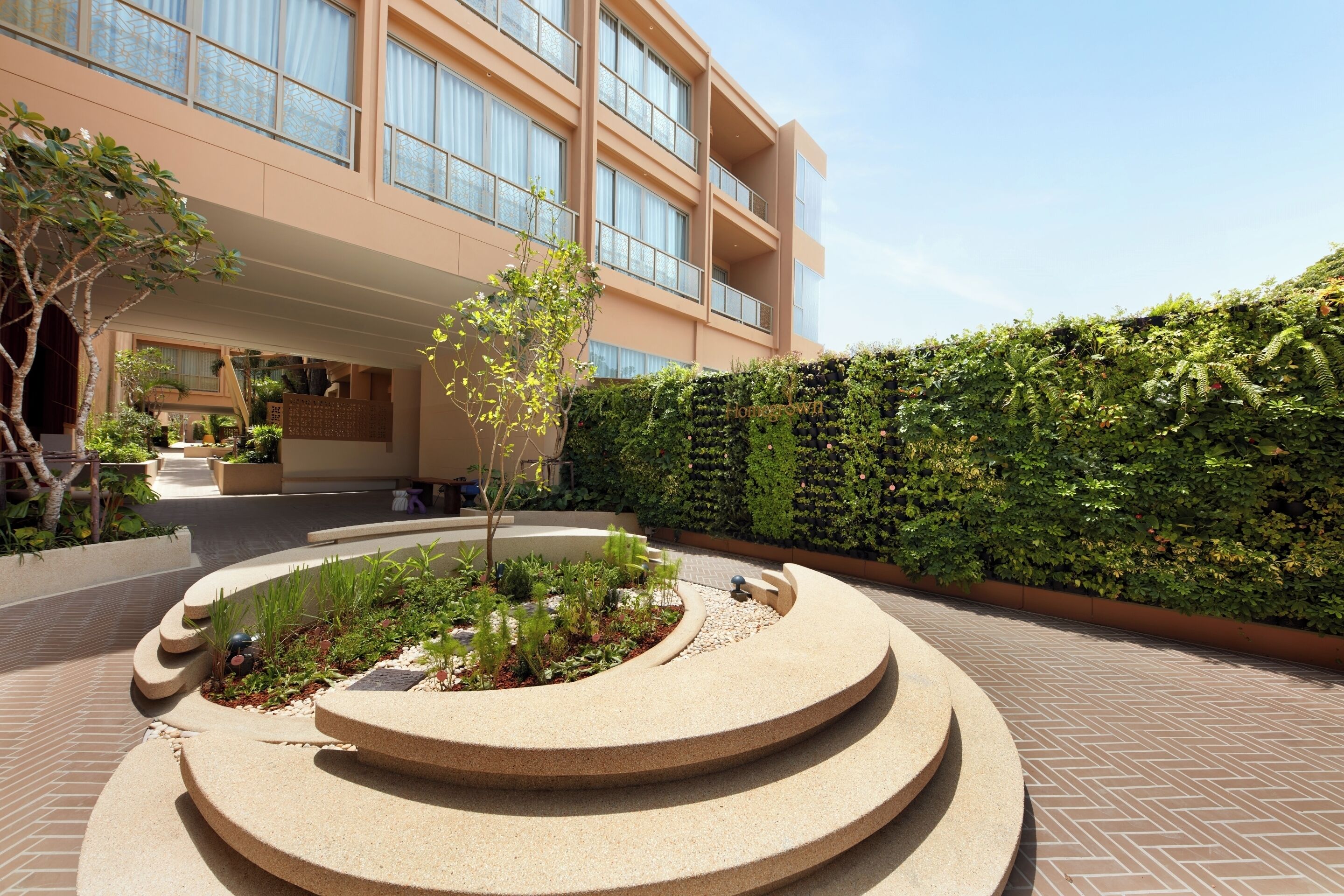 Um edifício moderno com um pátio ajardinado, apresentando um jardim circular com plantas e um hedge lateral.