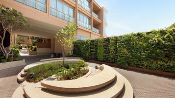 Um edifício moderno com um pátio ajardinado, apresentando um jardim circular com plantas e um hedge lateral.