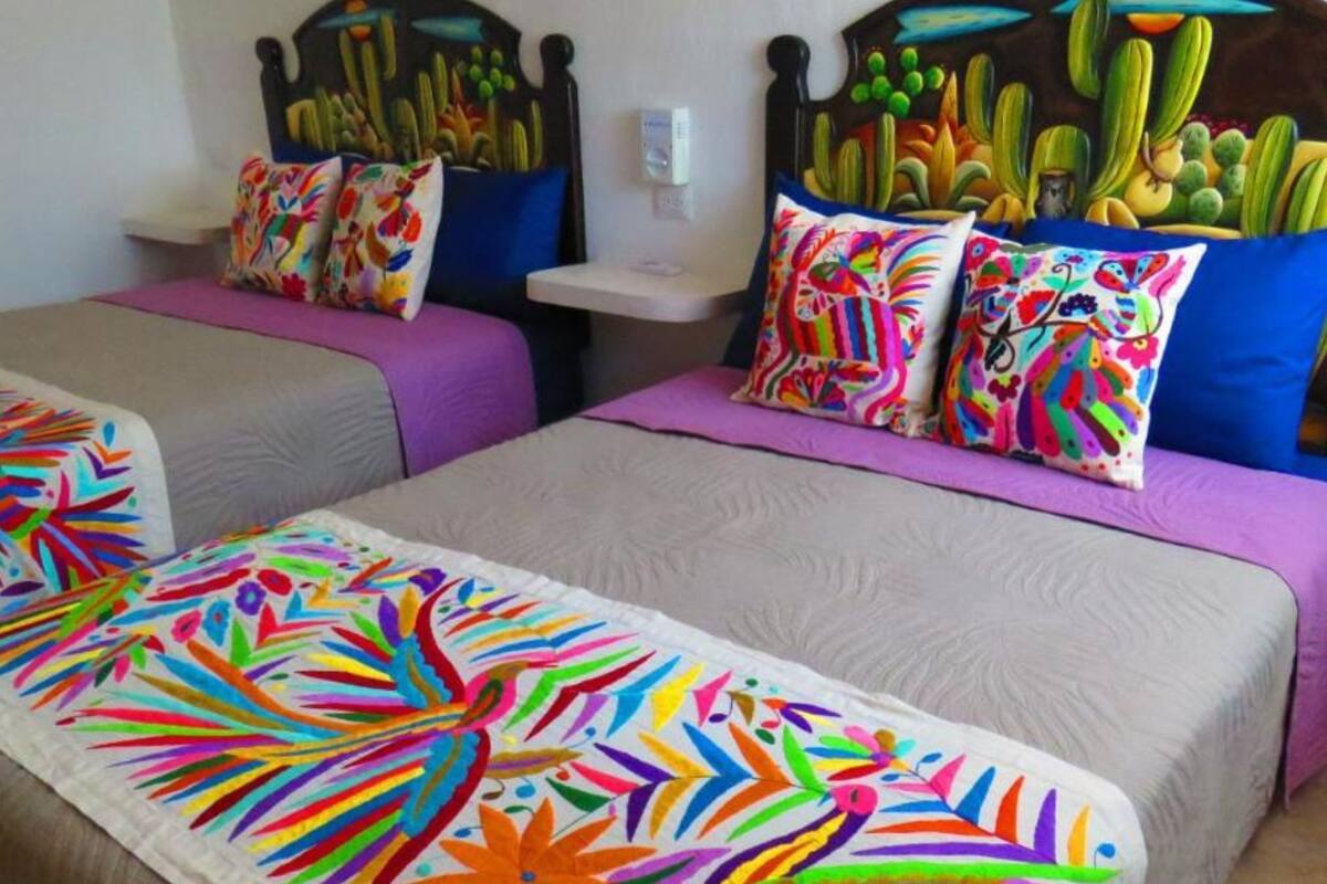 Quarto de hotel com duas camas, cada uma com cabeceira colorida e almofadas combinando.