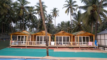 Uma fileira de cabanas de madeira com varandas, cercada por palmeiras e uma piscina.